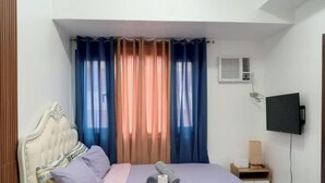 Quarto com cama, cortinas, aparelho de ar condicionado, televisão e mesa de cabeceira.