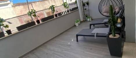 Um terraço no telhado com piso de madeira, uma cadeira suspensa e plantas em vasos.