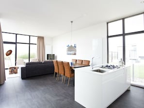 Uma cozinha moderna com uma ilha central, uma área de refeições com cadeiras, um sofá e uma televisão.