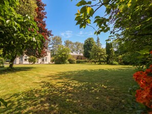 Um jardim bem cuidado com uma casa ao fundo, cercado por árvores e arbustos.
