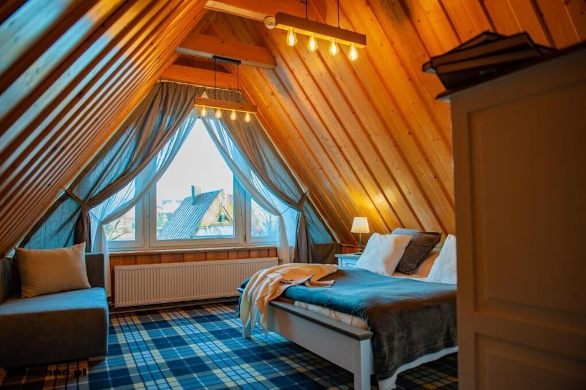 Um quarto de sótão aconchegante, com uma cama, uma cadeira e uma janela com cortinas.