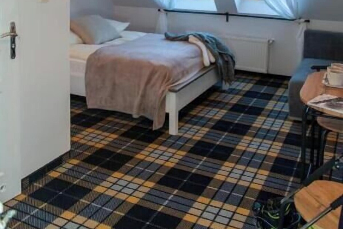 Quarto com cama, janela com cortinas, radiador e chão xadrez.