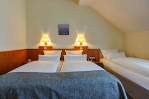 Quarto de hotel com duas camas, uma cabeceira de madeira, mesa de cabeceira, abajur e quadro pendurado na parede.