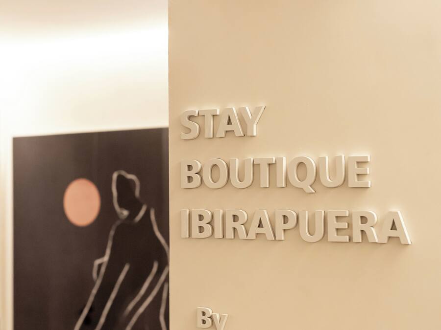 Paredes com um recorte em formato de olho de fechadura, o texto 'STAY BOUTIQUE IBIRAPUERA' e uma obra de arte em preto e branco, parcialmente visível.