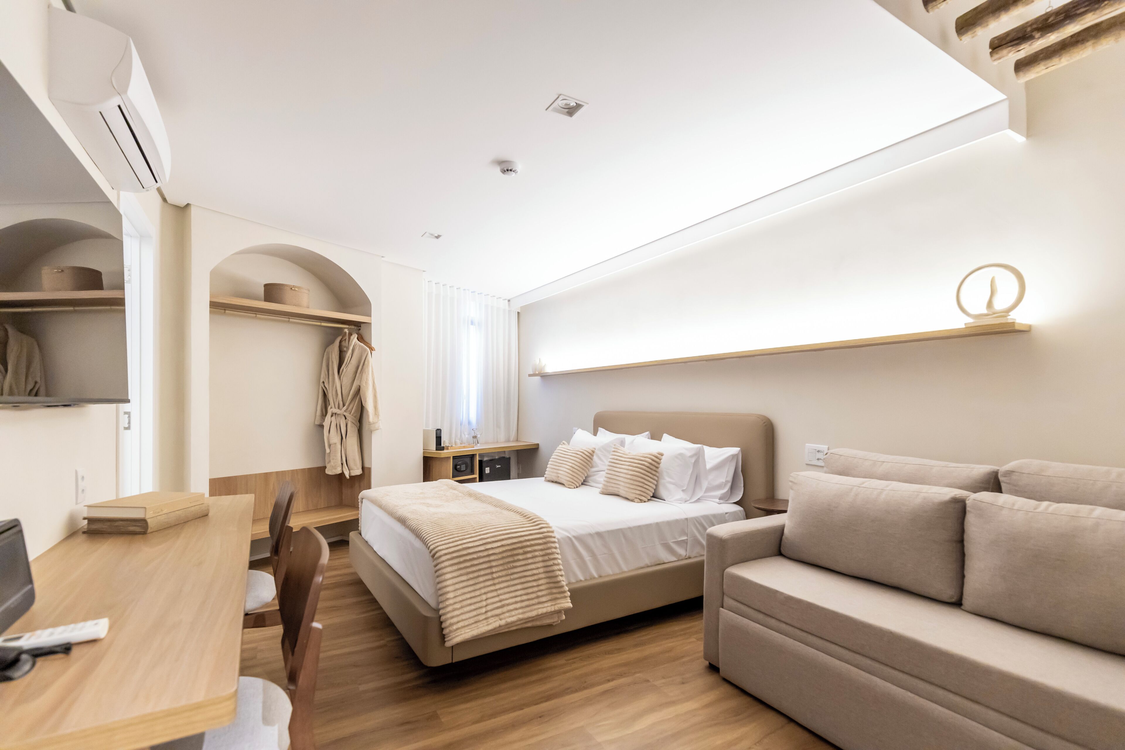 Quarto de hotel moderno com cama, sofá, escrivaninha e guarda-roupa.