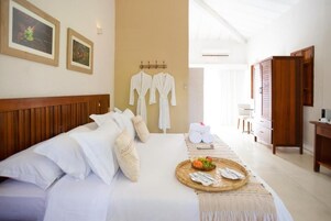 Quarto de hotel com cama, cabeceira de madeira, cabideiro fixado na parede, bandeja de café da manhã com frutas e guarda-roupa de madeira.