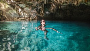 Uma pessoa nadando em uma piscina cristalina com paredes de caverna rochosa ao fundo.