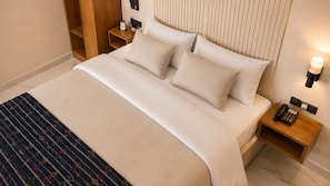 Quarto de hotel com cama, mesas de cabeceira, luminária e telefone.