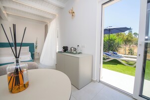 Quarto moderno com cama, mesa de cabeceira, armário pequeno e vista para um pátio exterior com mesa e cadeiras.
