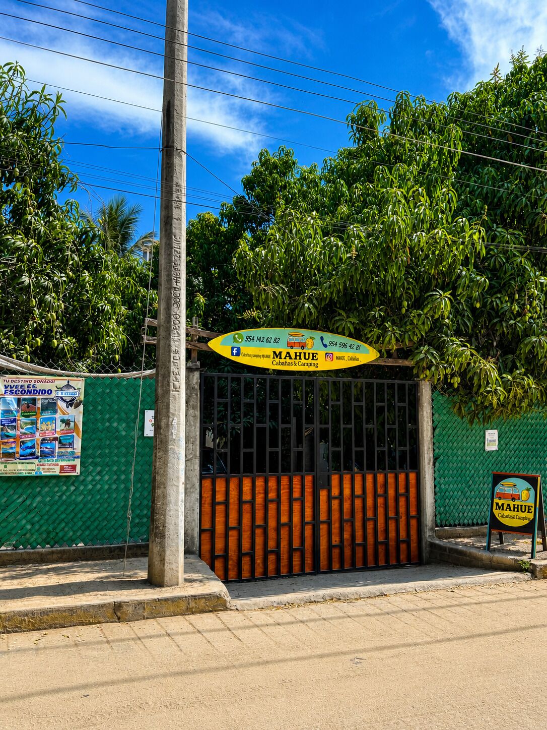 Uma entrada fechada com uma placa que diz 'MAHUE Cabanas & Camping' e uma cerca verde.