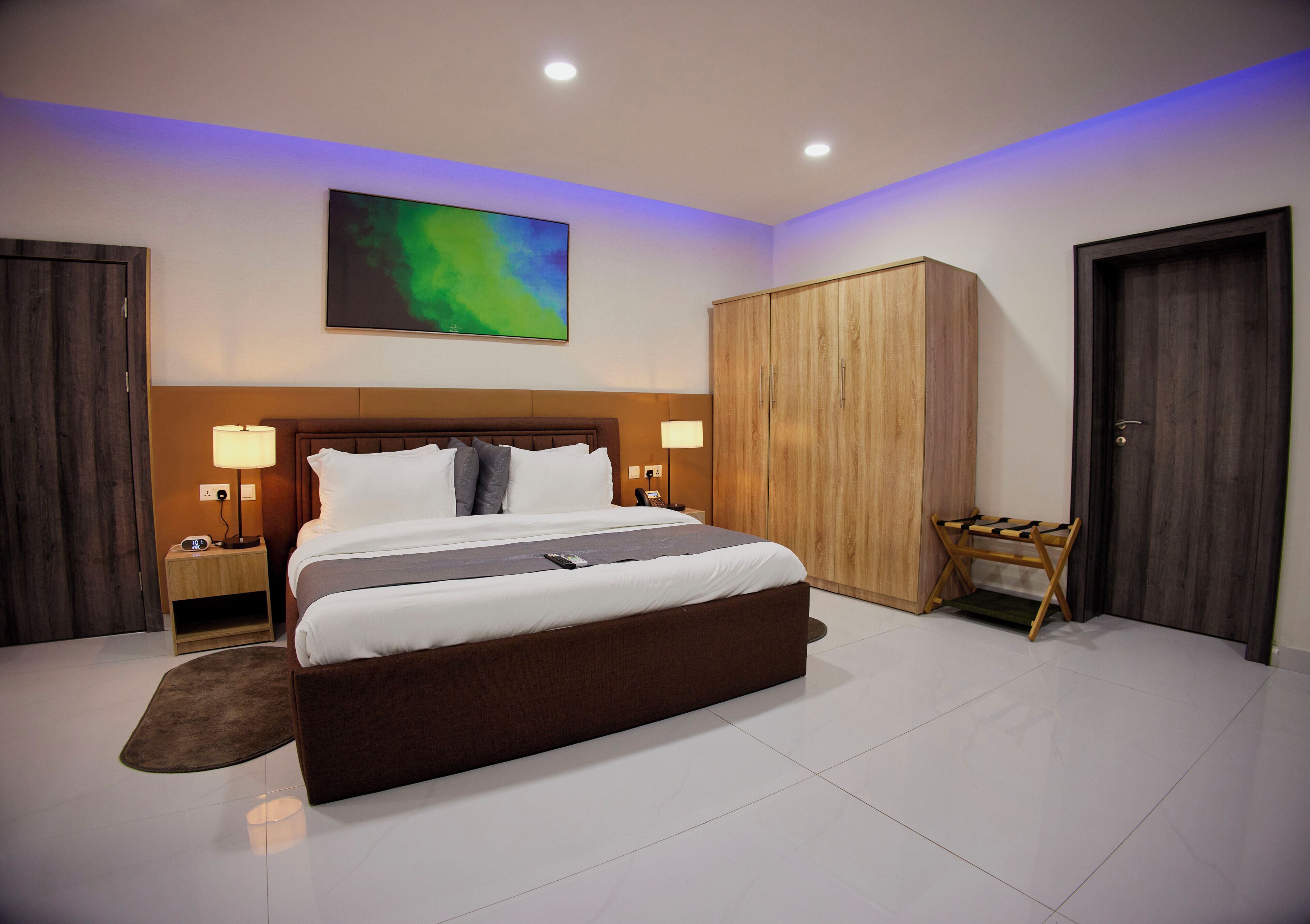 Quarto de hotel moderno com uma cama grande, luminárias de cabeceira, um guarda-roupa e um quadro na parede.