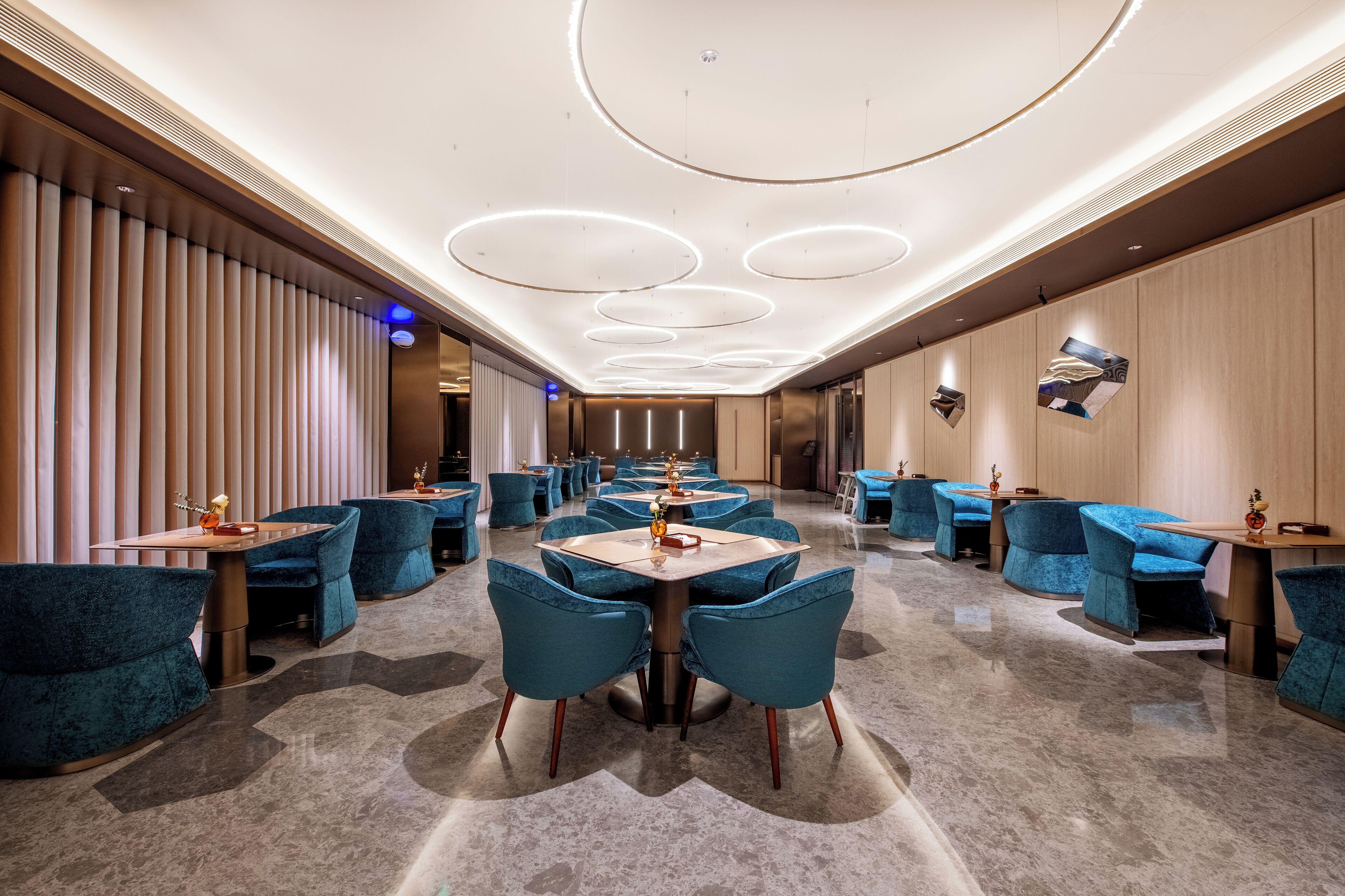 Um hall de hotel moderno com mesas redondas, cadeiras estofadas em azul e piso de mármore polido.