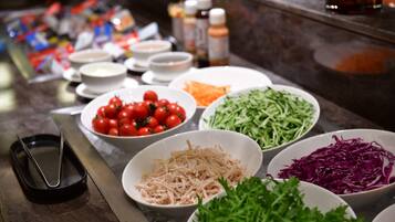 Mesa de buffet com diversos alimentos, incluindo tomates, frango desfiado e folhas verdes.