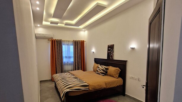 Quarto com cama, luminária no teto, ar-condicionado fixado na parede e uma porta.