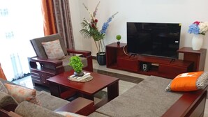 Uma sala de estar moderna com um conjunto de sofá, uma mesa de centro, televisão e plantas decorativas.