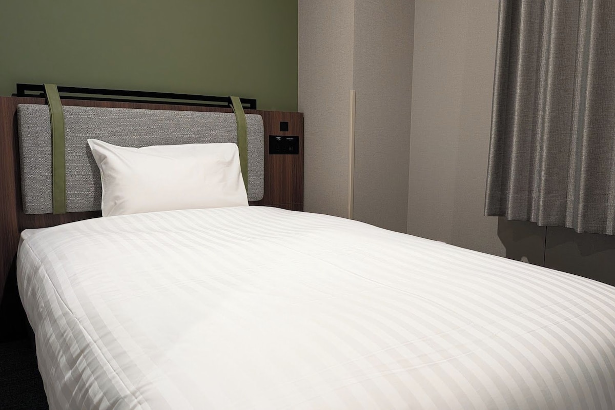 Quarto de hotel com cama, cabeceira e cortinas.