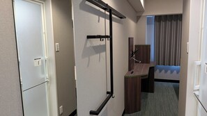 Quarto de hotel com uma cama, escrivaninha, cadeira, guarda-roupa e janela com cortinas.