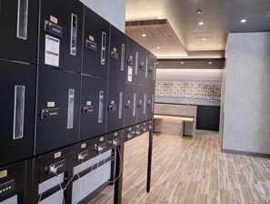 Fileira de armários pretos com etiquetas numeradas, teto de madeira com iluminação embutida e parede com padrão ao fundo.