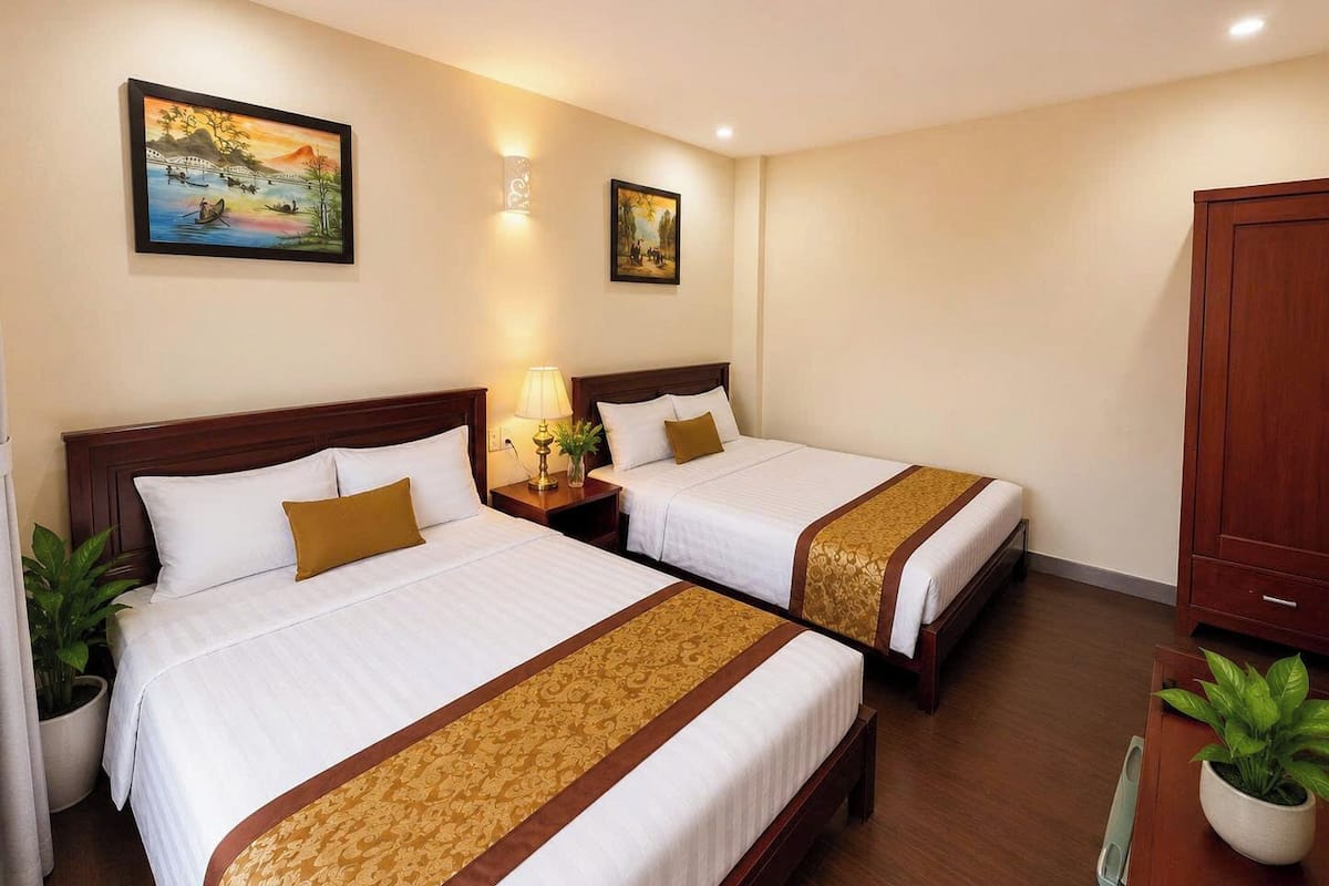 Quarto de hotel com duas camas, uma mesa de cabeceira com abajur, um guarda-roupa e duas pinturas penduradas na parede.