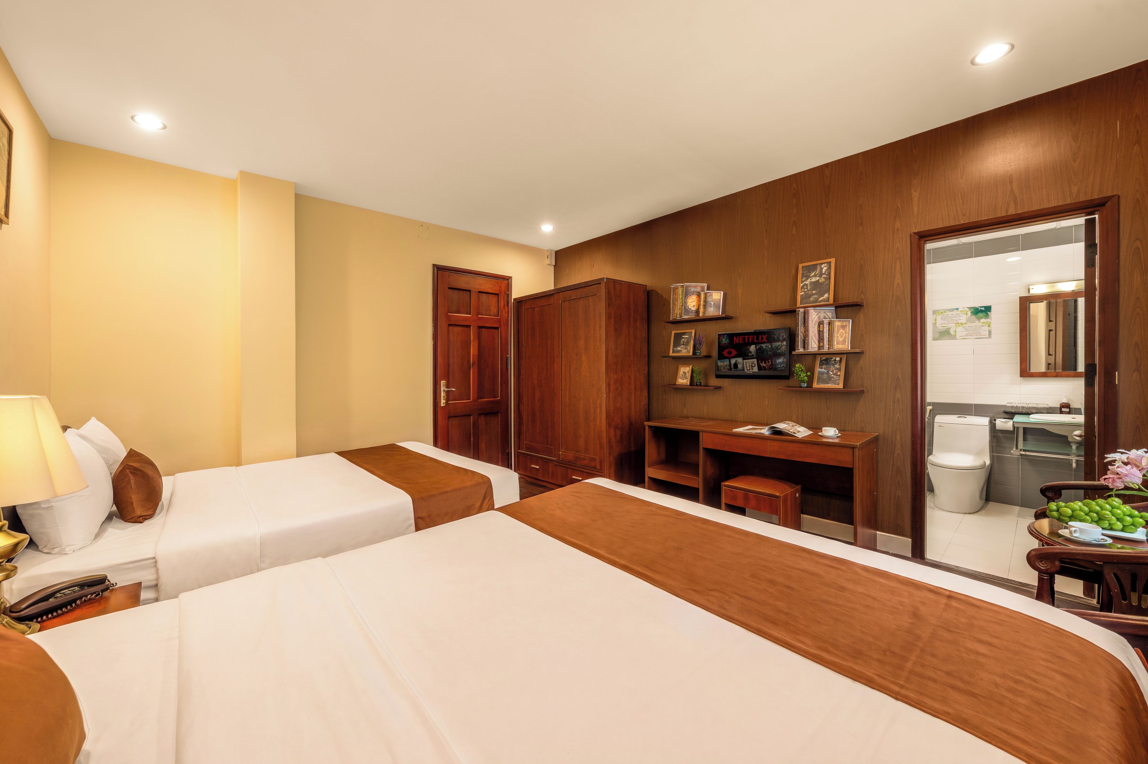 Quarto de hotel com duas camas, uma escrivaninha, guarda-roupa, banheiro e uma pequena área de refeições.