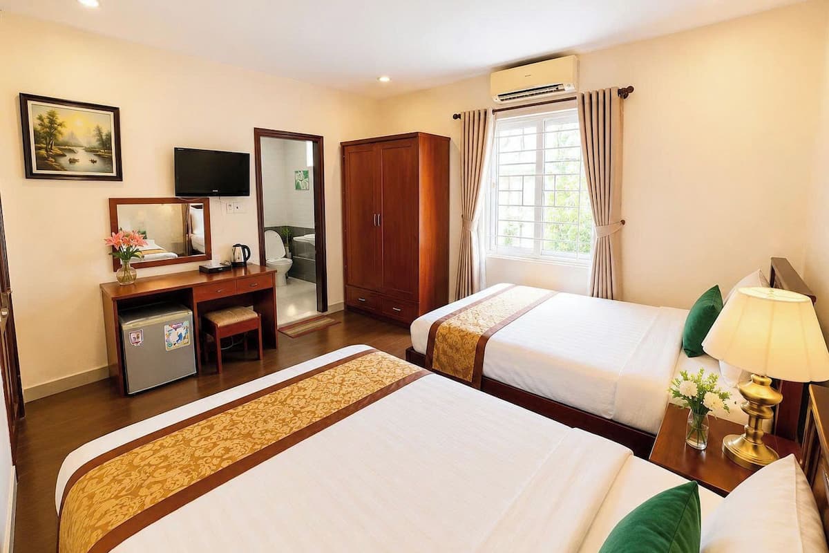 Quarto de hotel com duas camas, uma escrivaninha com computador, TV, guarda-roupa e janela com cortinas.