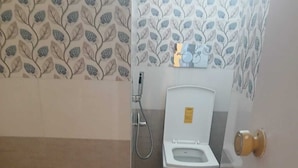 Casa de banho com sanita, chuveiro e papel de parede estampado.