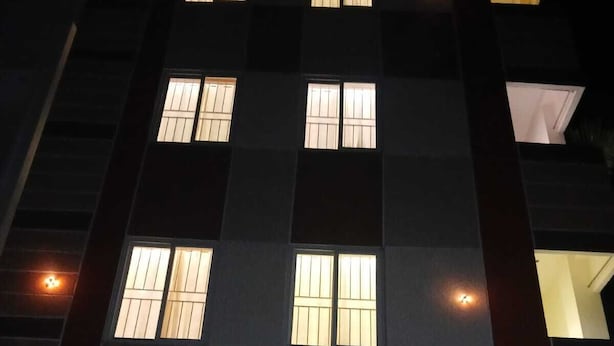 Um edifício com vários andares, janelas iluminadas, entrada com portão e área coberta com guarda-corpo.