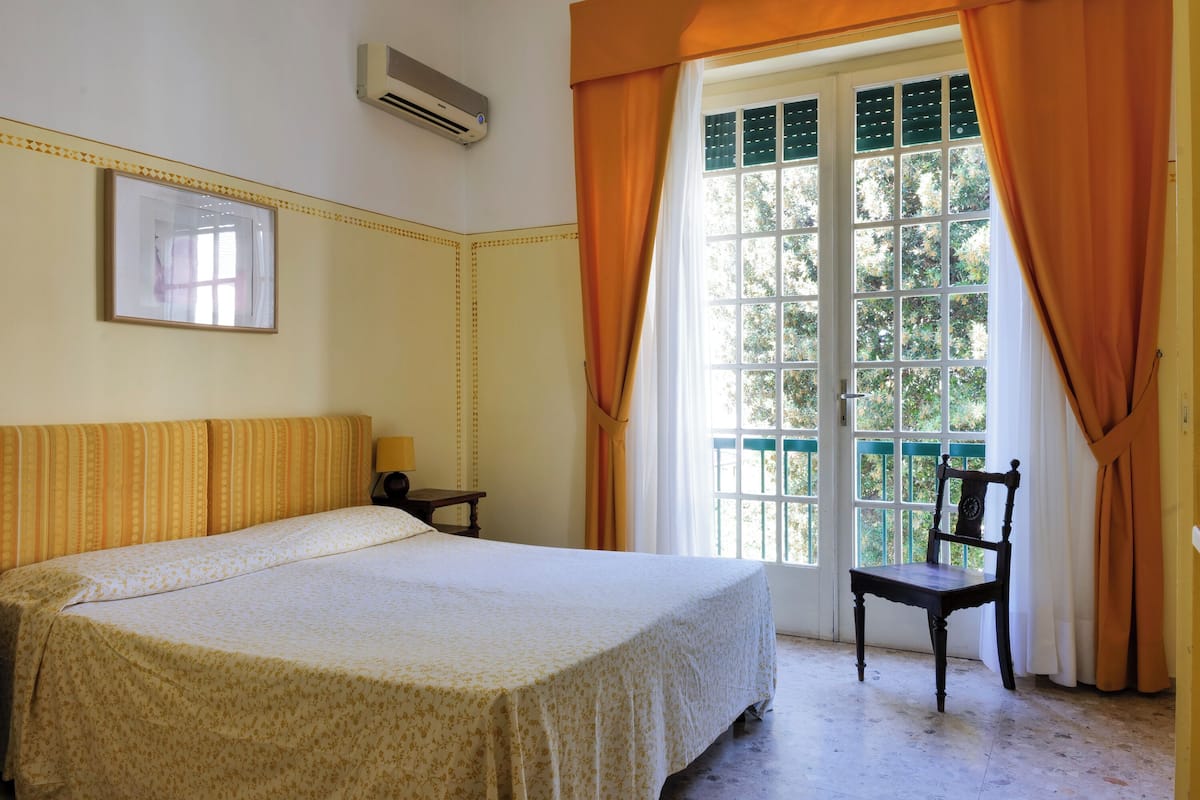 Quarto com cama, cadeira, janela com cortinas e ar condicionado.