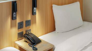 Quarto de hotel com cabeceira de madeira, telefone ao lado da cama, tomada e janela.