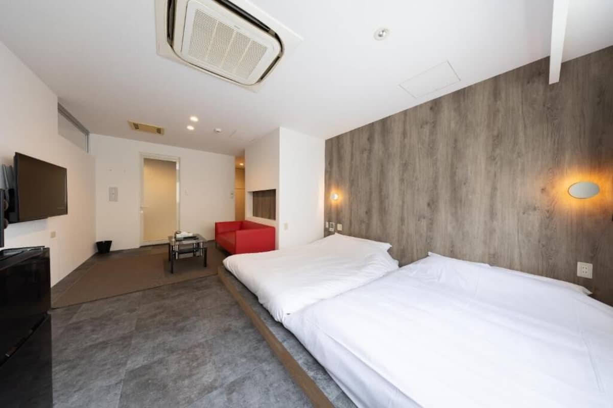 Quarto de hotel com uma cama, uma cadeira vermelha, uma televisão e uma parede de destaque em madeira.