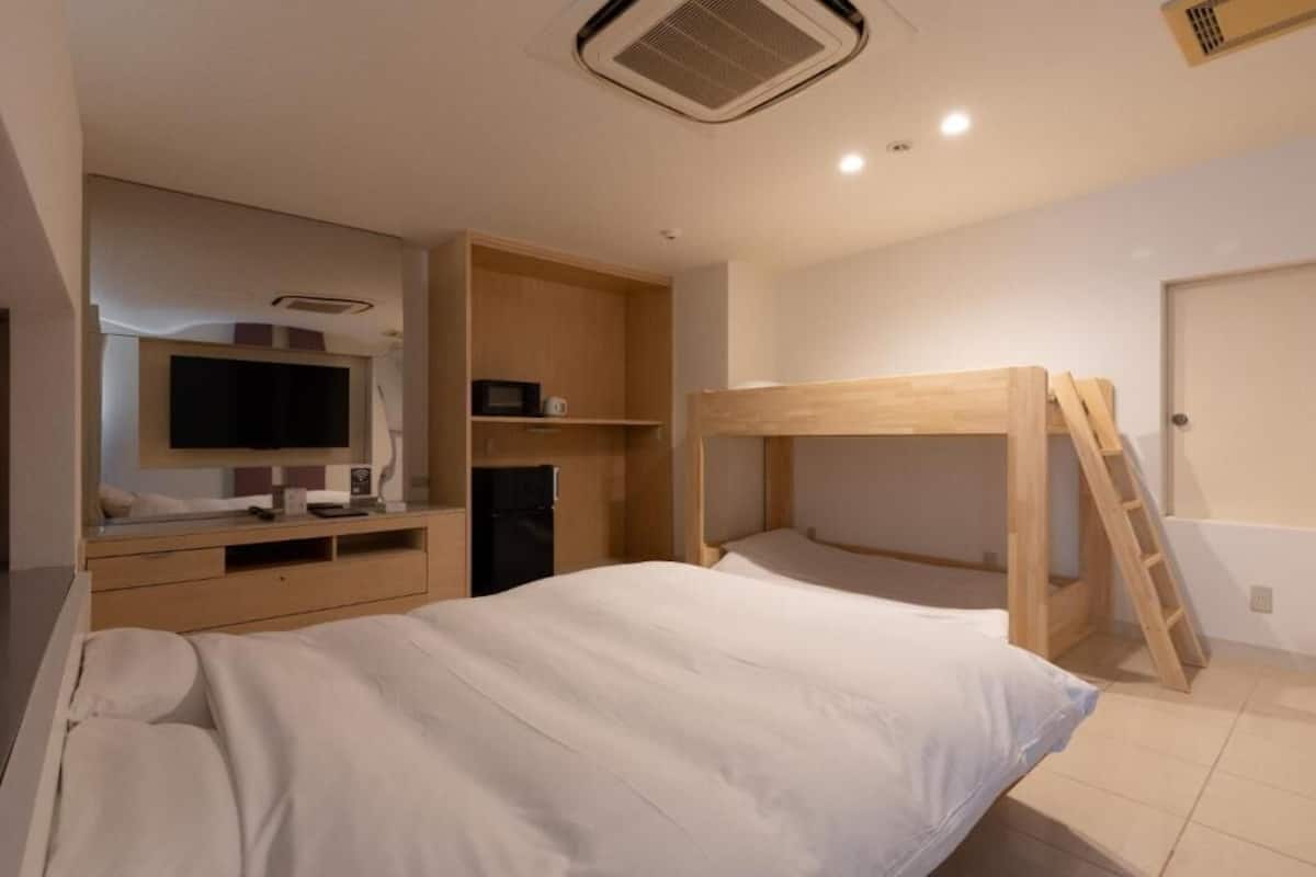 Quarto com cama de solteiro, televisão, escrivaninha e guarda-roupa.