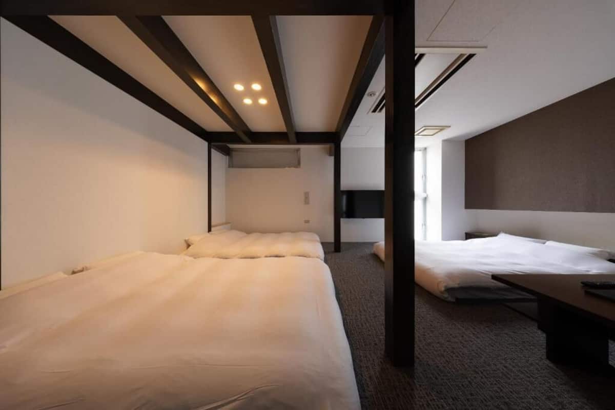 Quarto de hotel com duas camas, uma escrivaninha e uma janela grande.