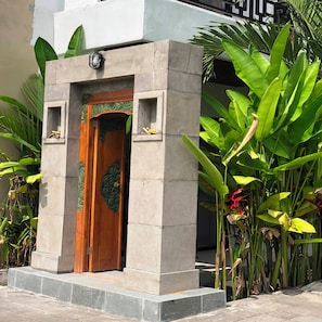 Uma construção de pedra com porta de madeira, rodeada por plantas tropicais.