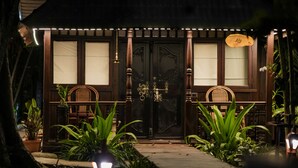 Uma casa de madeira tradicional com uma porta de entrada escura, duas cadeiras de vime e uma pequena mesa na varanda.