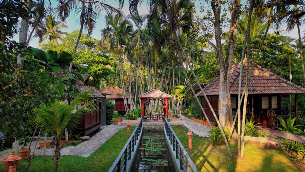 Um resort tropical com um canal, palmeiras e cabanas tradicionais.