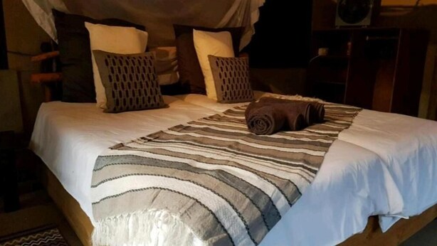 Uma cama com um cobertor listrado, várias almofadas e uma toalha enrolada.