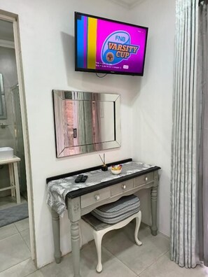 Quarto com toucador, televisão fixada na parede e espelho em cima.