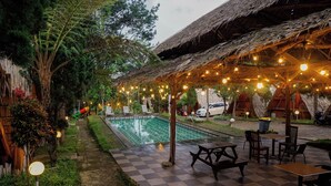 Uma área ao lado da piscina com piso xadrez, móveis de madeira e luzes de corda.