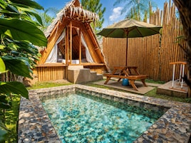 Uma estrutura de madeira com telhado de palha, piscina com água cristalina e cerca de bambu.
