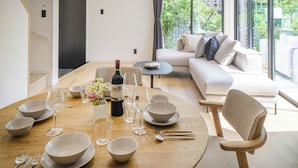 Uma área de refeições moderna com uma mesa de madeira posta para uma refeição, um sofá e vista para o verde lá fora.