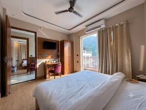 Quarto de hotel com cama, escrivaninha, cadeira, ventilador de teto, aparelho de ar condicionado e vista para o exterior.