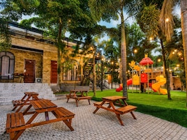 Um pátio com mesas de piquenique, uma área de recreação com escorregadores e um edifício com fachada de tijolos.