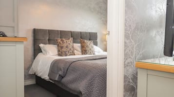 Quarto com cama, cabeceira e parede com padrão de árvore.