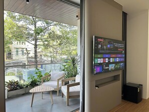 Varanda com uma televisão exibindo diversos aplicativos, uma cadeira branca e uma mesa pequena.