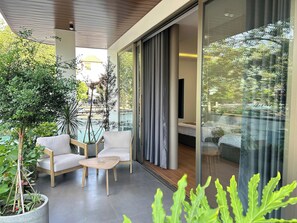 Uma sala de estar moderna com uma porta de vidro que dá para uma varanda, uma mesa de madeira, dois sofás brancos e diversas plantas de interior.
