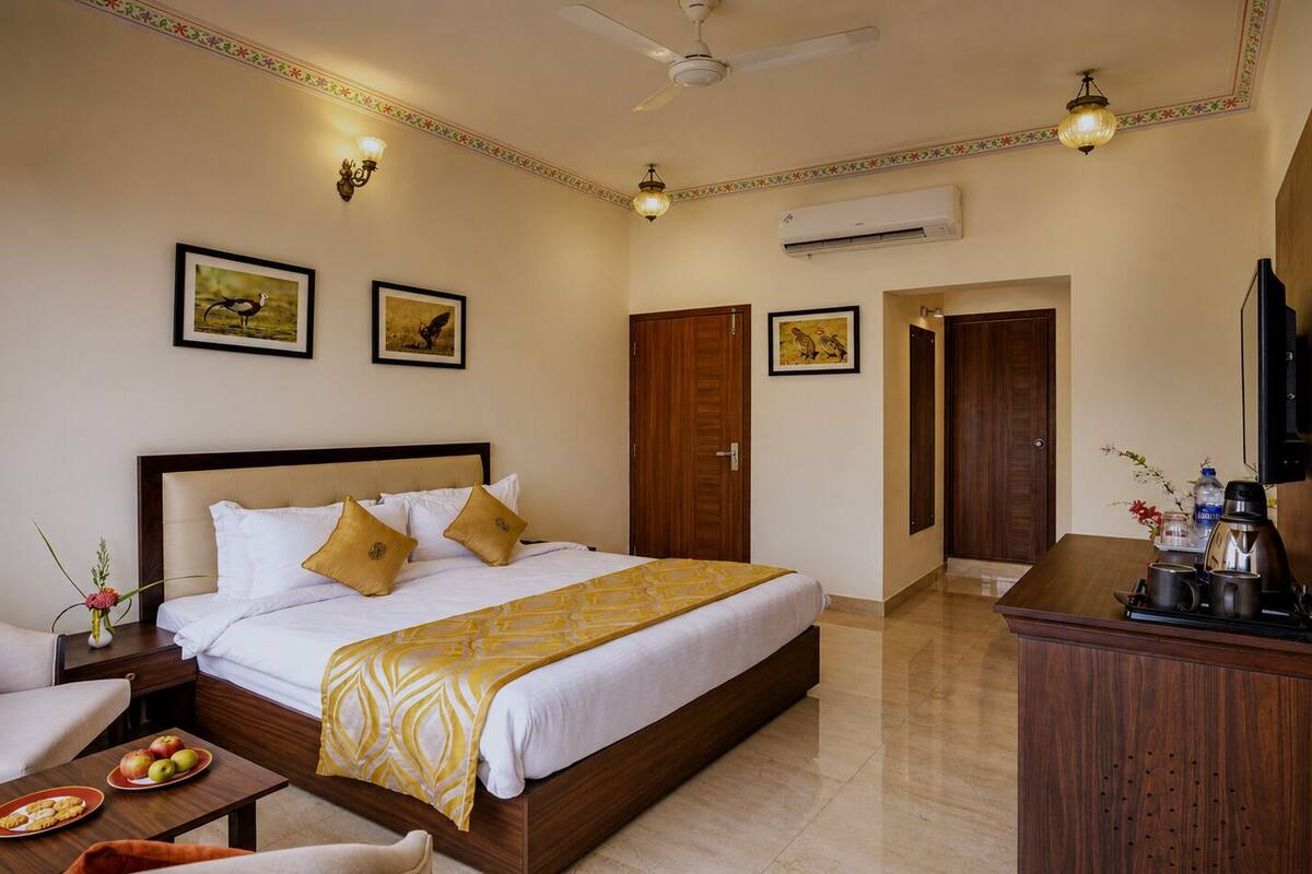 Quarto de hotel com cama, escrivaninha, cadeira, televisão e minibar.