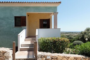 Uma casa com parede de pedra, um conjunto de degraus levando a um alpendre, e vista para o campo.