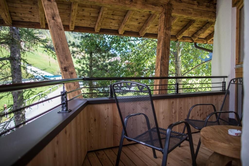 Uma área externa coberta com vigas de madeira, cadeiras de metal e uma mesa.