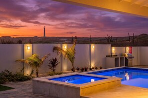 Piscina com vista para um farol, cercada por um jardim paisagístico e área de churrasco.