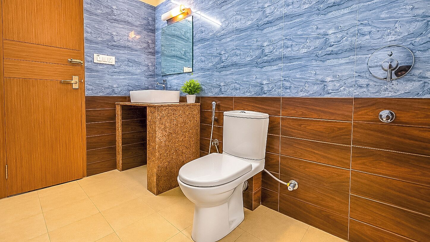 Casa de banho com toucador de madeira, sanita branca e parede revestida a azulejos azuis.